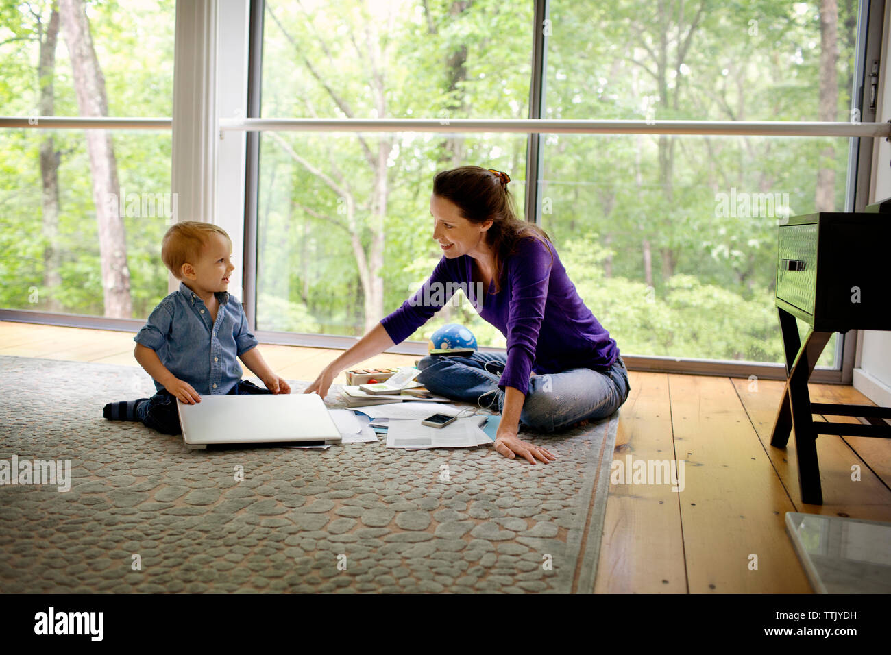 Mother doing paperwork looking at son sitting with laptop computer on ...