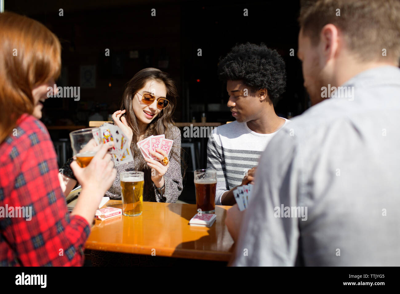 Smiling friends playing cards while having beer at table in brewery ...