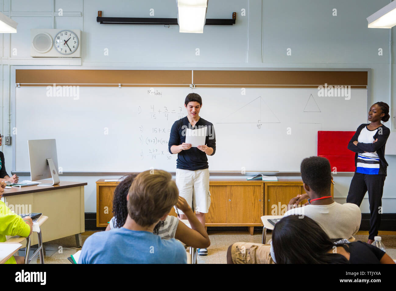 Teacher looking at student reading paper during in lesson in classroom ...