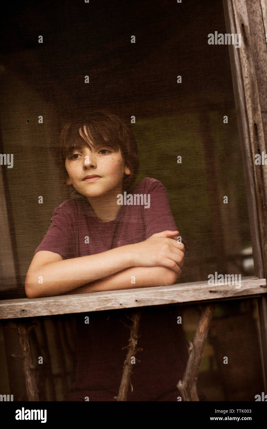 Boy looking away while leaning on window sill in tree house Stock Photo ...