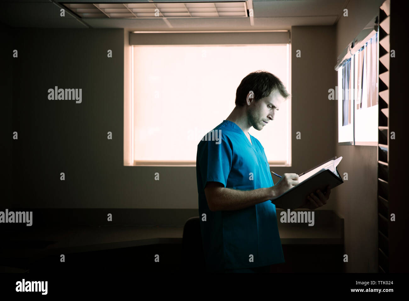 Doctor writing report while standing in hospital ward Stock Photo - Alamy
