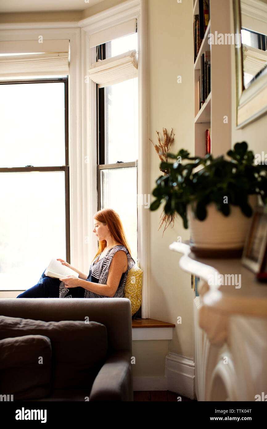 Woman reading book while sitting on alcove window seat at home Stock ...