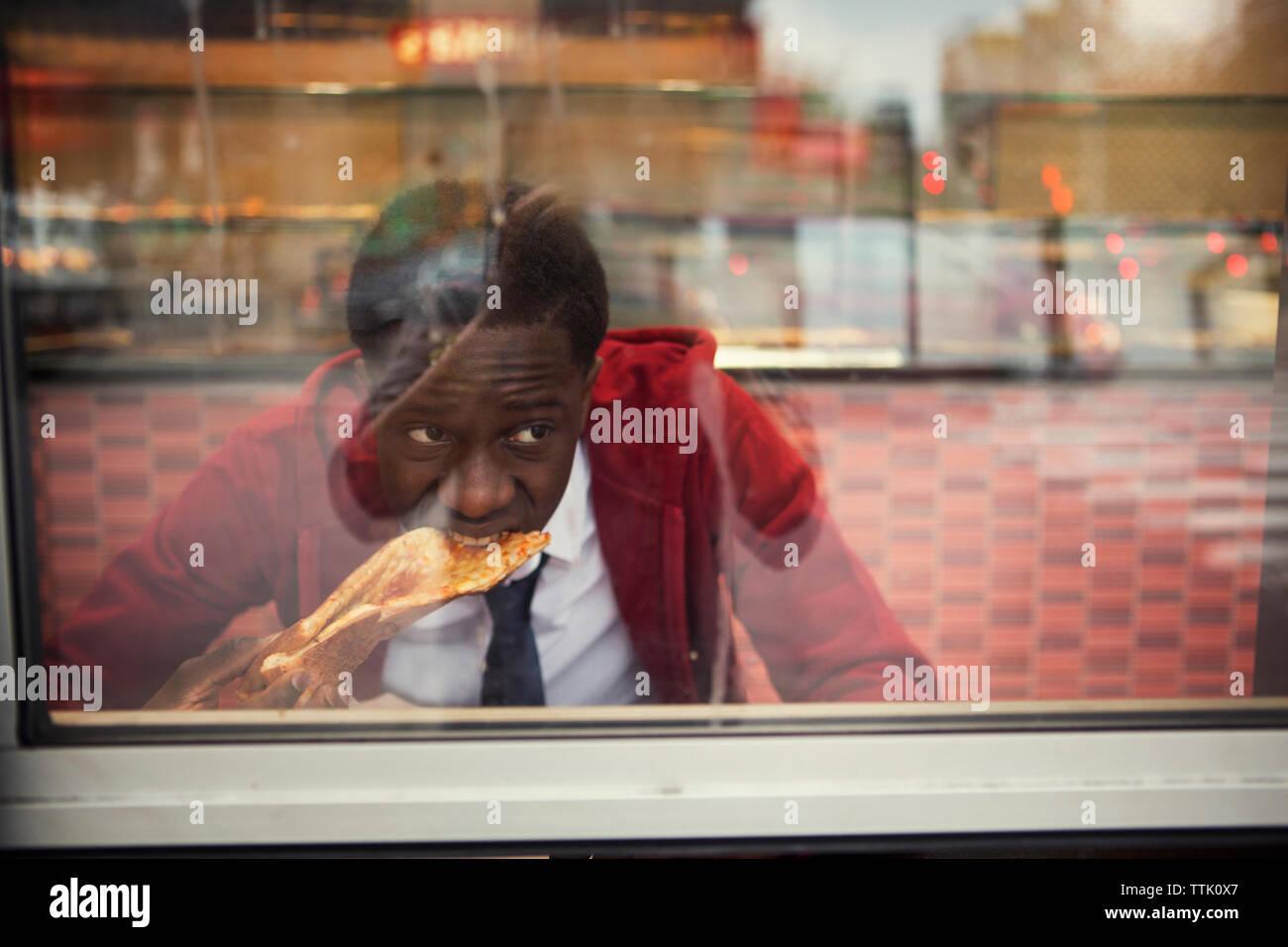 student eating pizza seen through window with reflection of city Stock ...