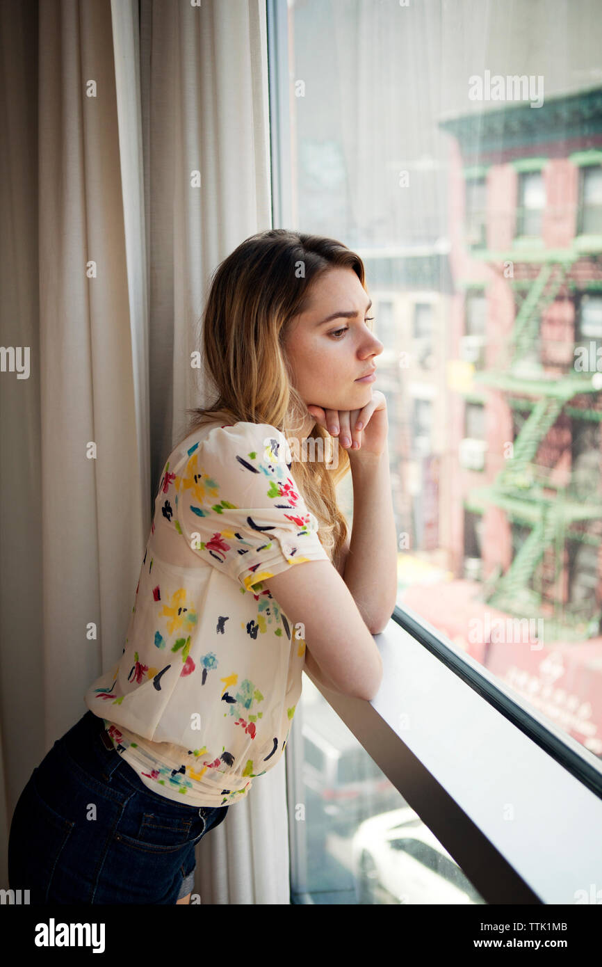 Thoughtful woman looking through window while standing at home Stock ...