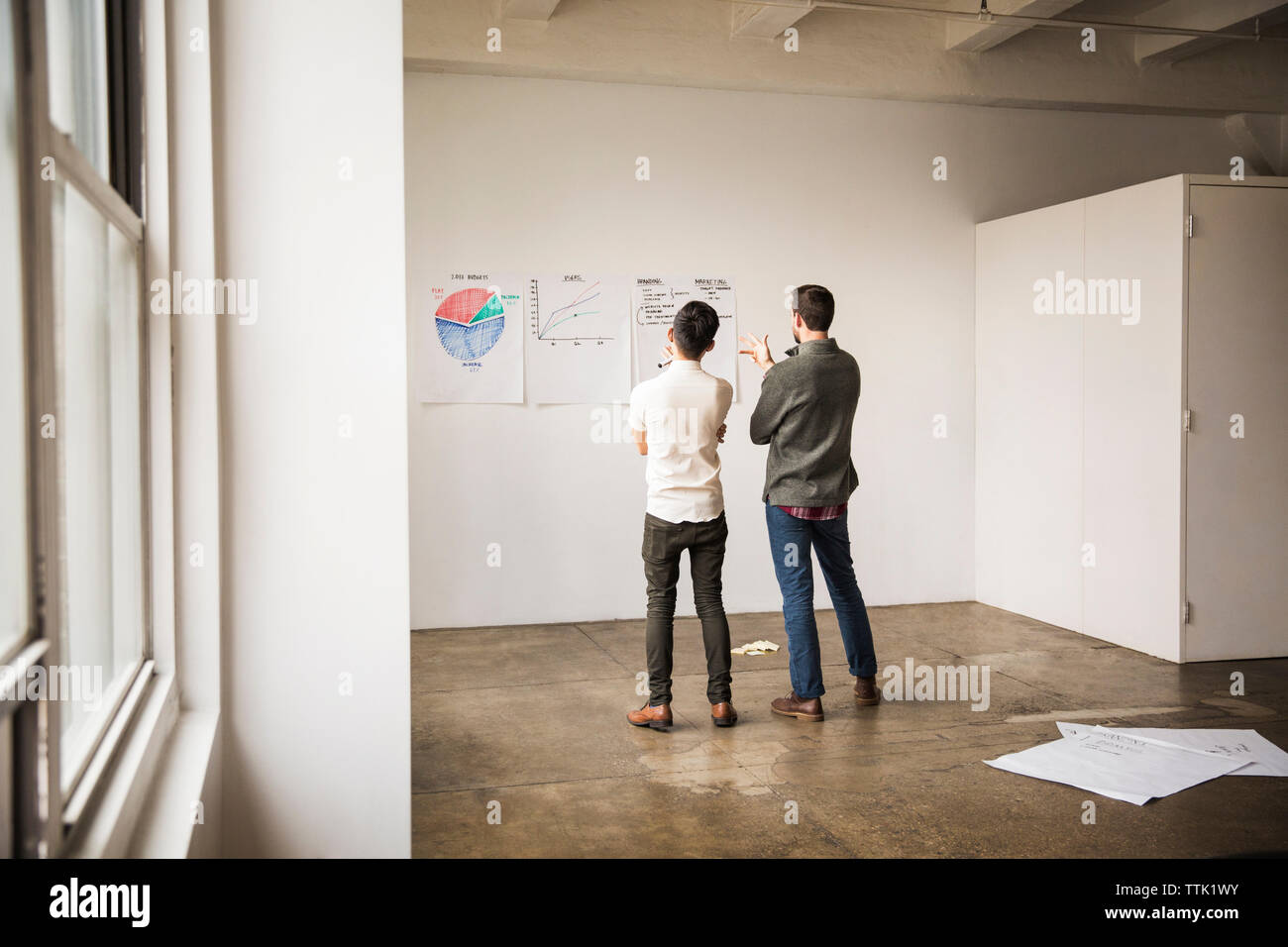 Rear view of business colleagues looking at charts while standing in ...