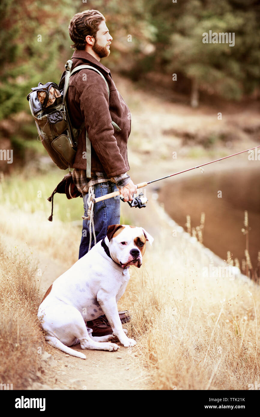 Side view of traveler fishing while sitting with dog at lakeshore Stock ...