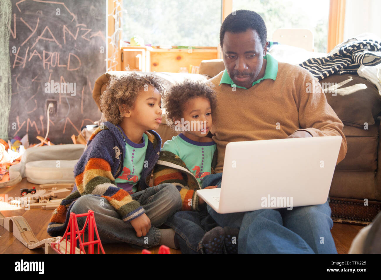 Father showing laptop computer to children while sitting on floor at ...