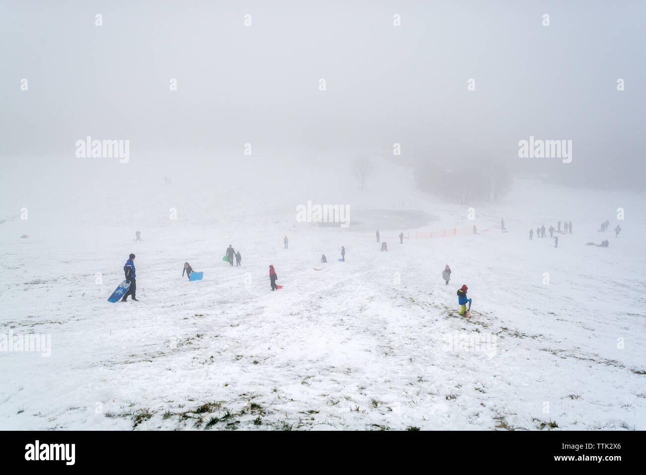 People enjoying snow skating on the slope on foggy morning after snow ...
