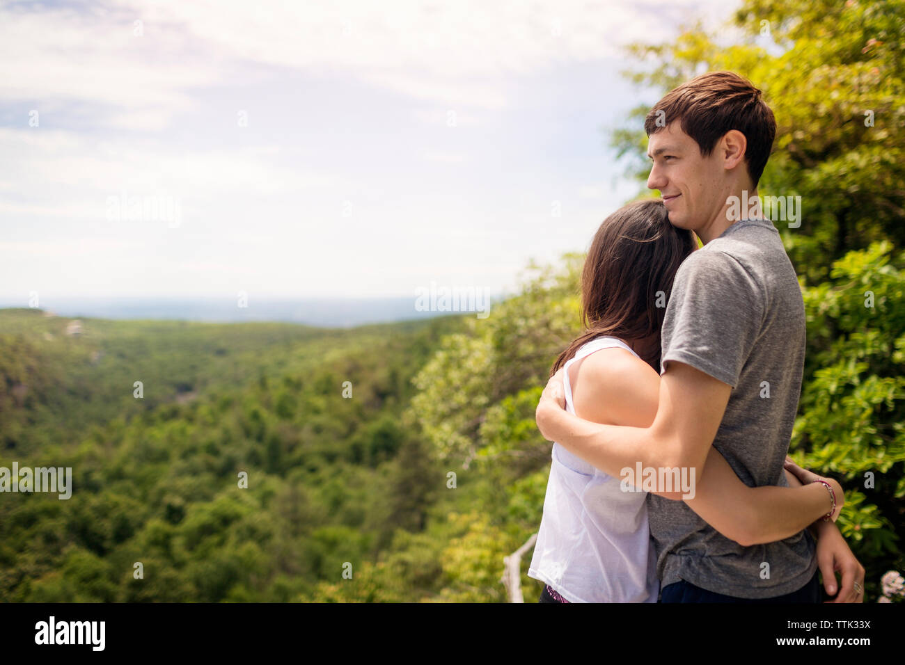 Side view of man embracing woman while standing against trees Stock ...