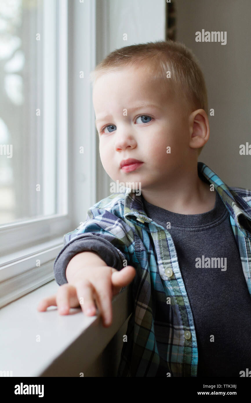 Portrait of cute boy standing by window at home Stock Photo - Alamy