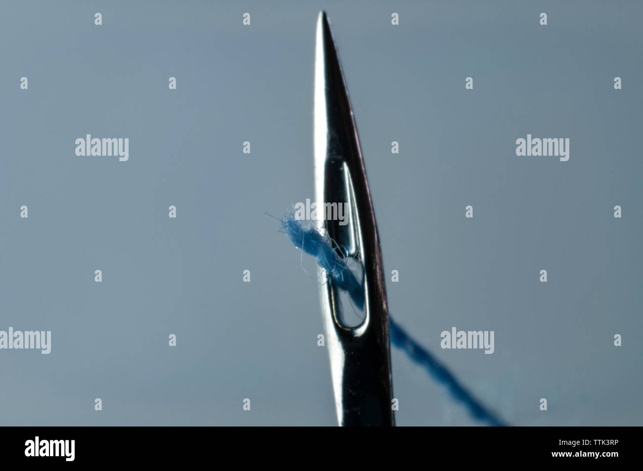macrophotography of an eye of a sewing machine needle with blue yarn ...
