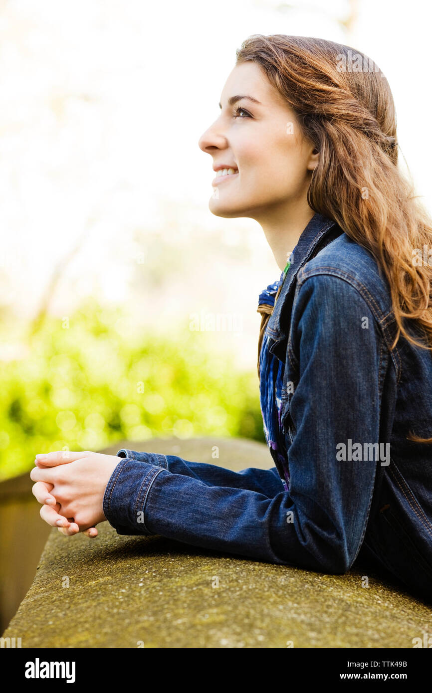 Side view of woman resting on retaining wall against sky Stock Photo ...