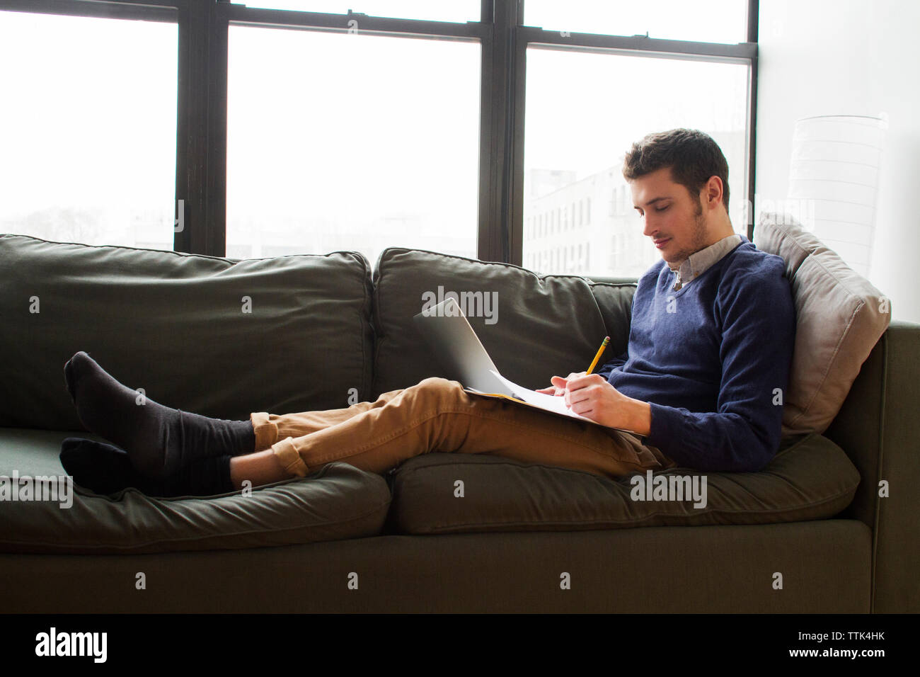 Side view of man using laptop and writing while sitting by windows ...