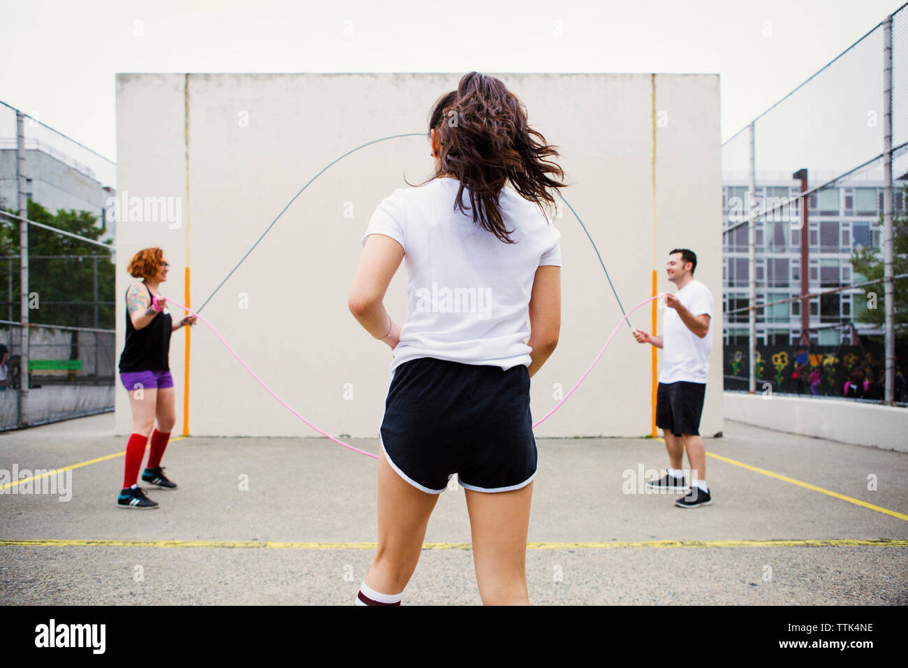 Woman walking towards friends holding jump ropes on street against wall ...