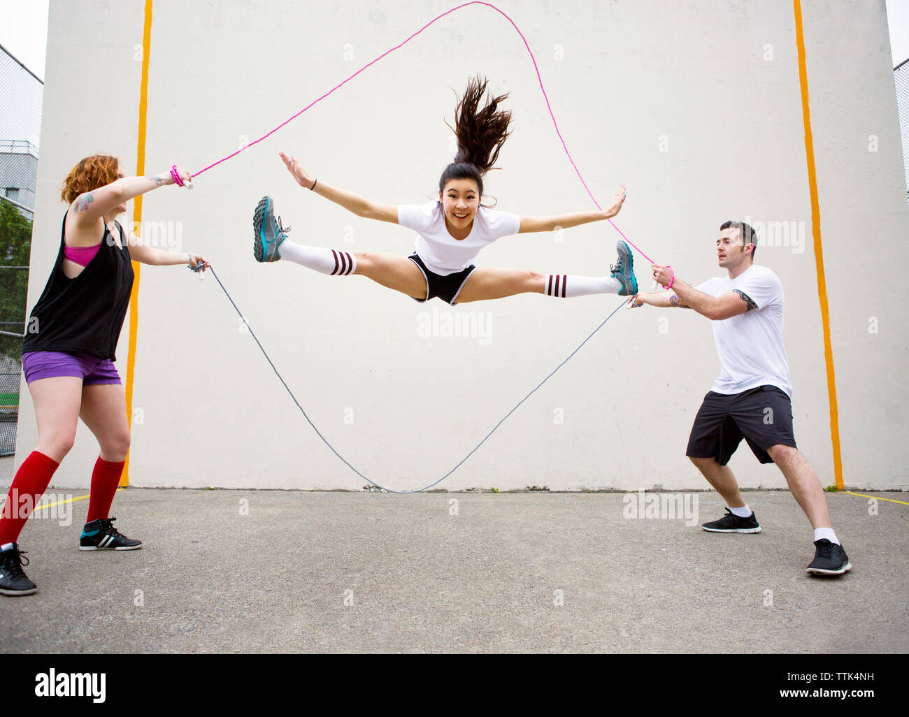 Confident woman doing splits while performing double Dutch against wall ...