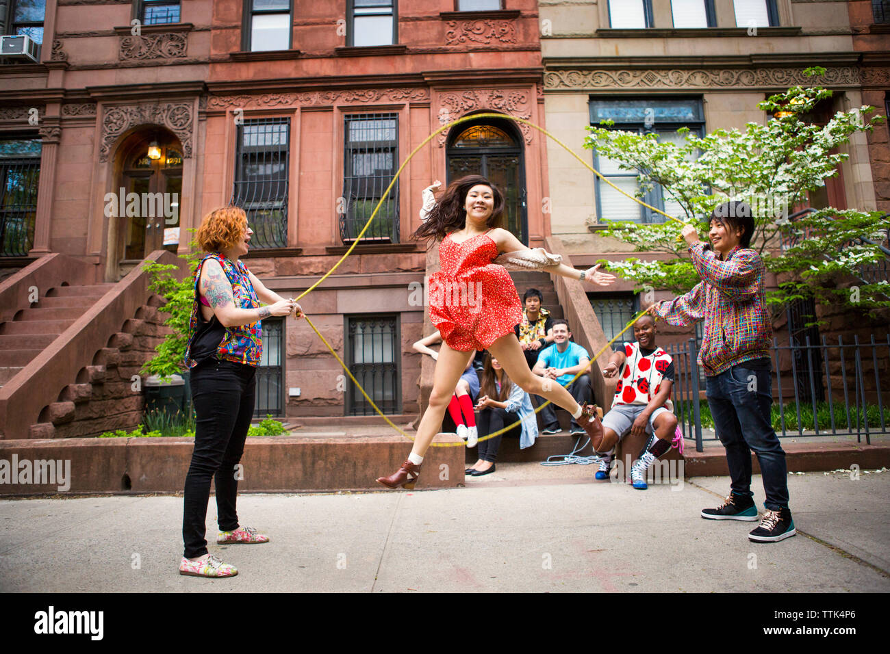 Friends looking at woman performing double Dutch on sidewalk against ...