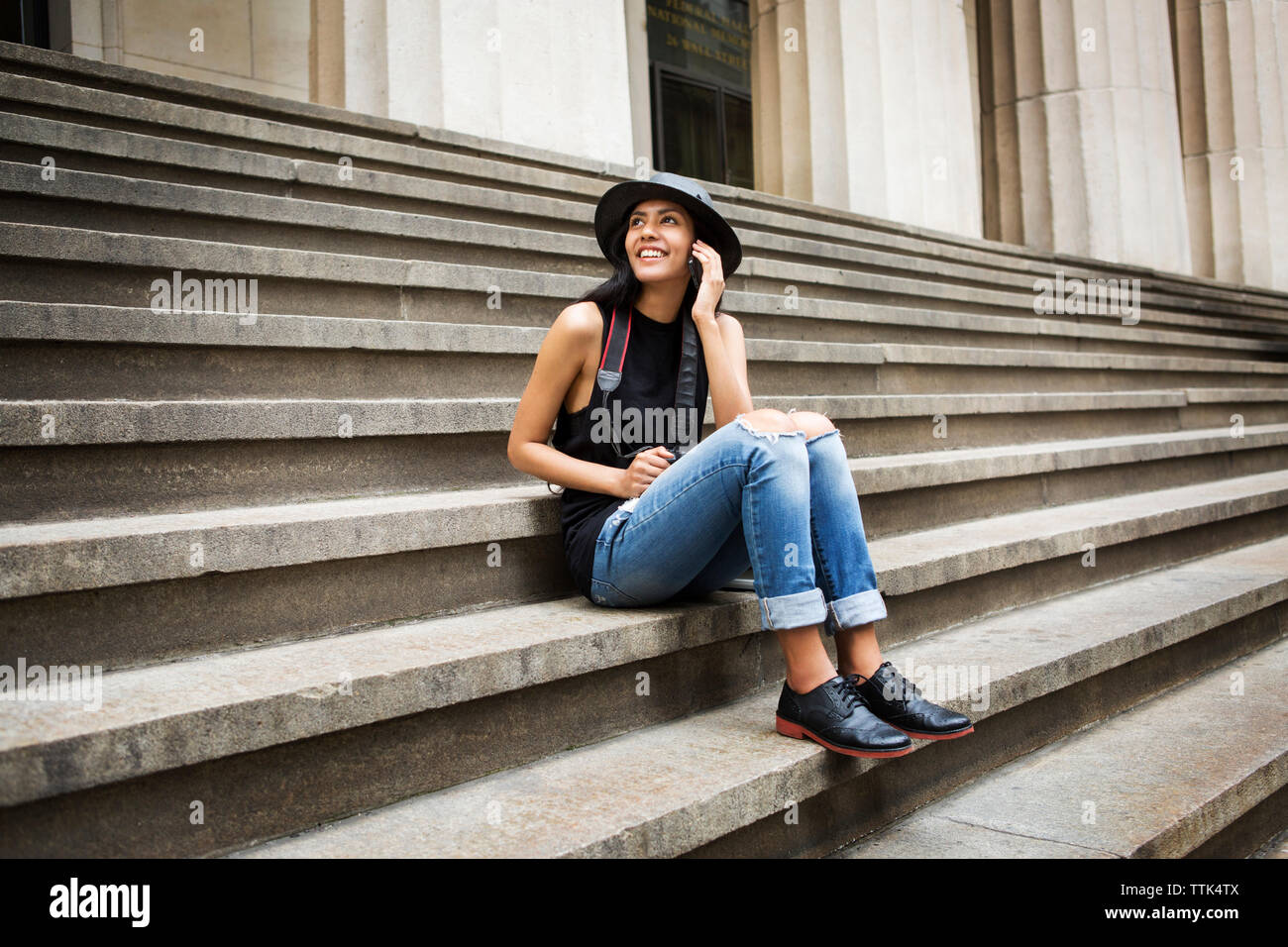 Smiling woman talking on phone while sitting on steps Stock Photo - Alamy