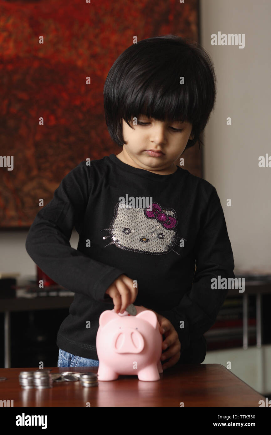 Indian girl putting a coin into a piggy bank Stock Photo - Alamy