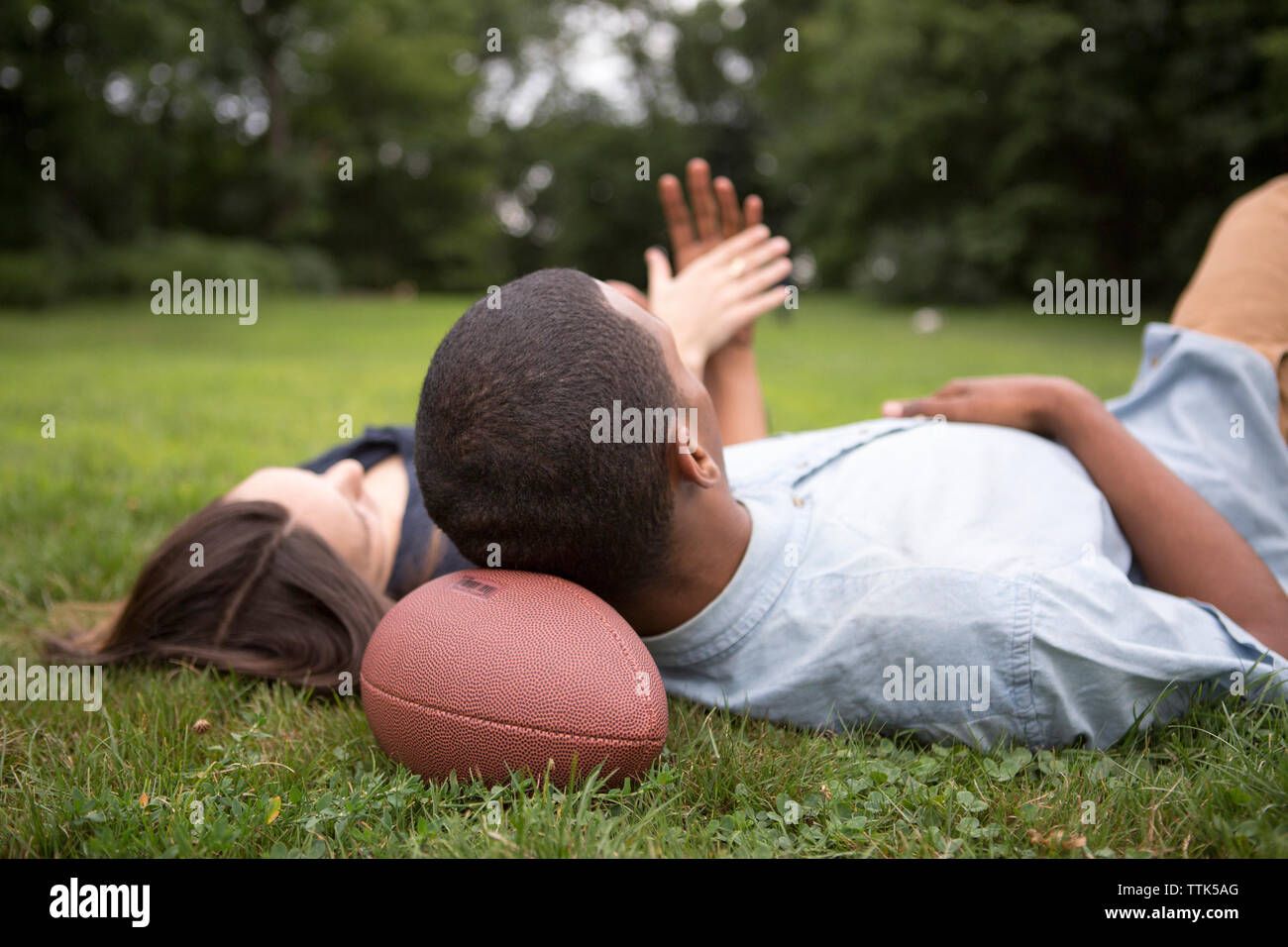 Man resting head on football ball while lying with woman on field Stock ...