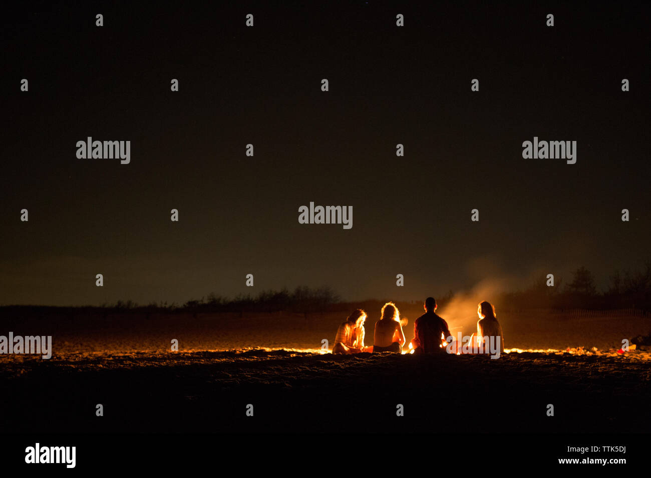 Friends sitting around bonfire at beach during night Stock Photo - Alamy