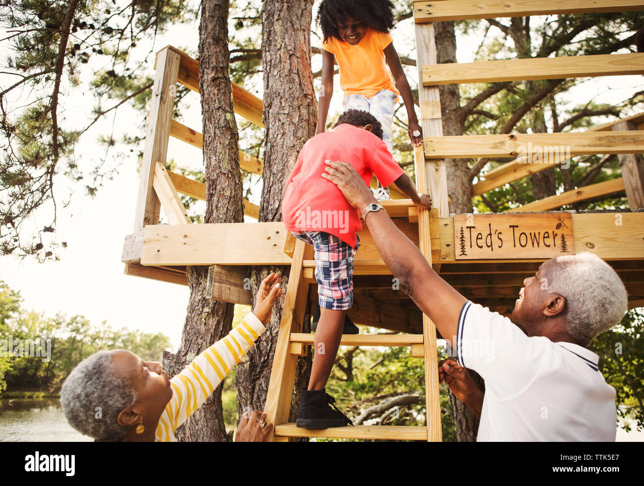 Grandparents assisting grandson in climbing steps of tree house Stock ...