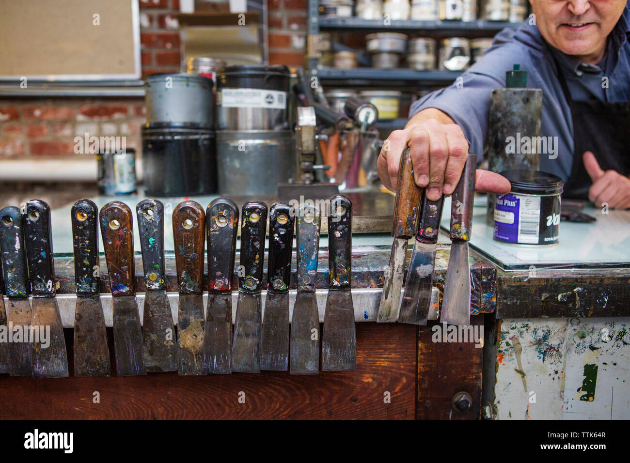 Man picking ink knives by table in workshop Stock Photo - Alamy