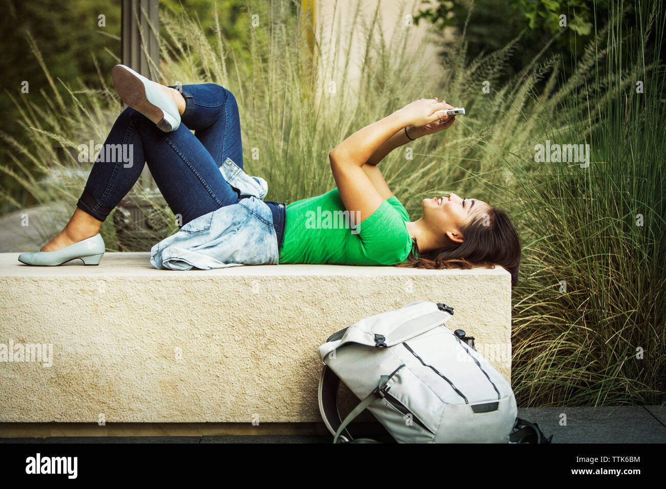 Woman using mobile phone while lying on concrete bench Stock Photo - Alamy