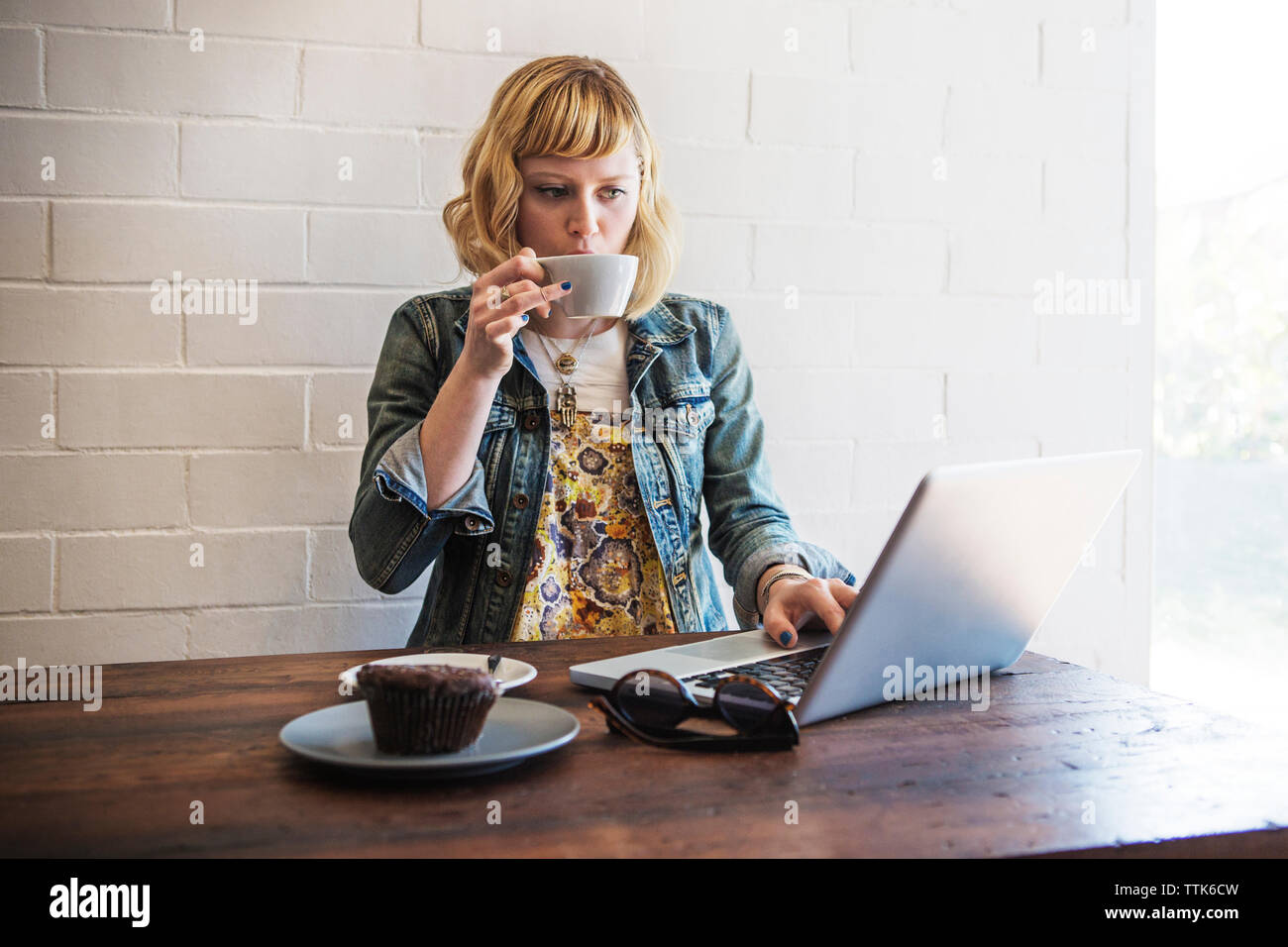 Woman drinking coffee while using laptop computer in cafe Stock Photo ...