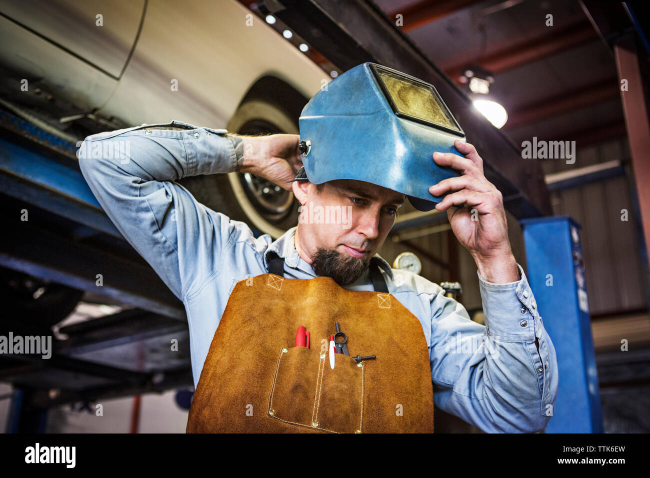 Mechanic wearing welding helmet while standing at auto repair shop ...