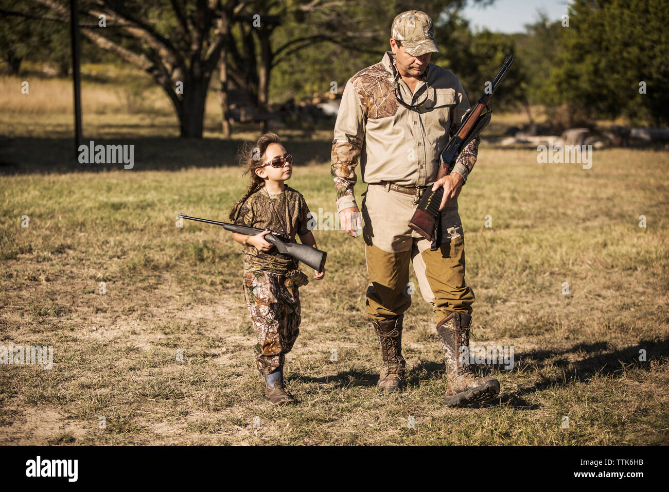 Hunters holding rifle while walking on grassy field Stock Photo - Alamy