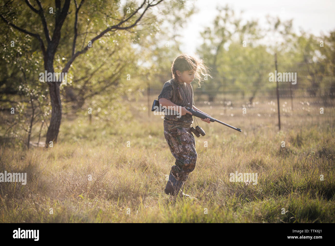 Girl holding rifle while walking on grassy field Stock Photo - Alamy