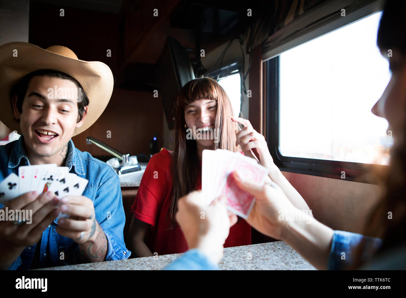Happy friends playing cards at table while travelling in camper van ...