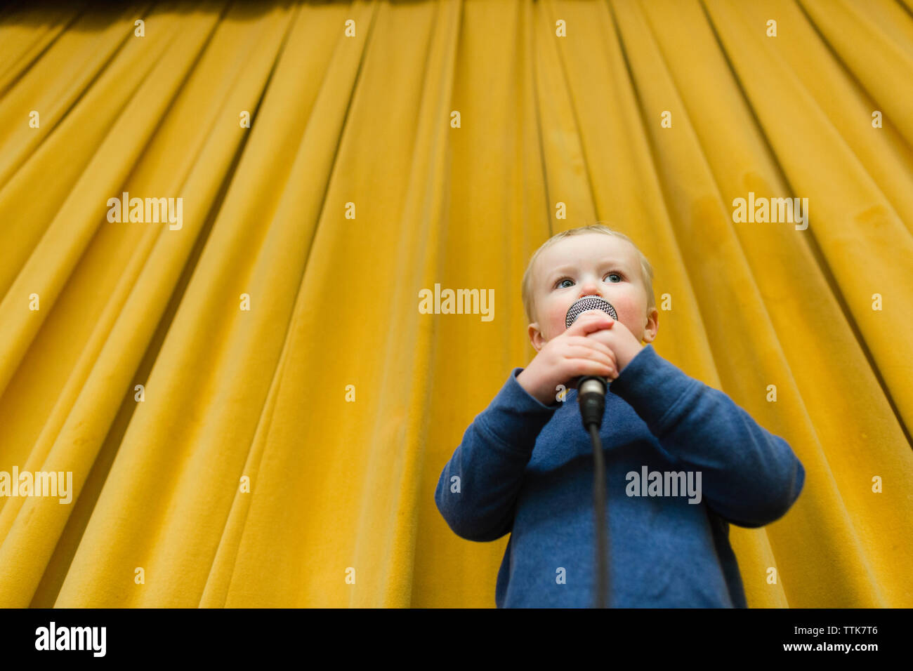 Low angle view of cute boy singing on microphone at stage against ...