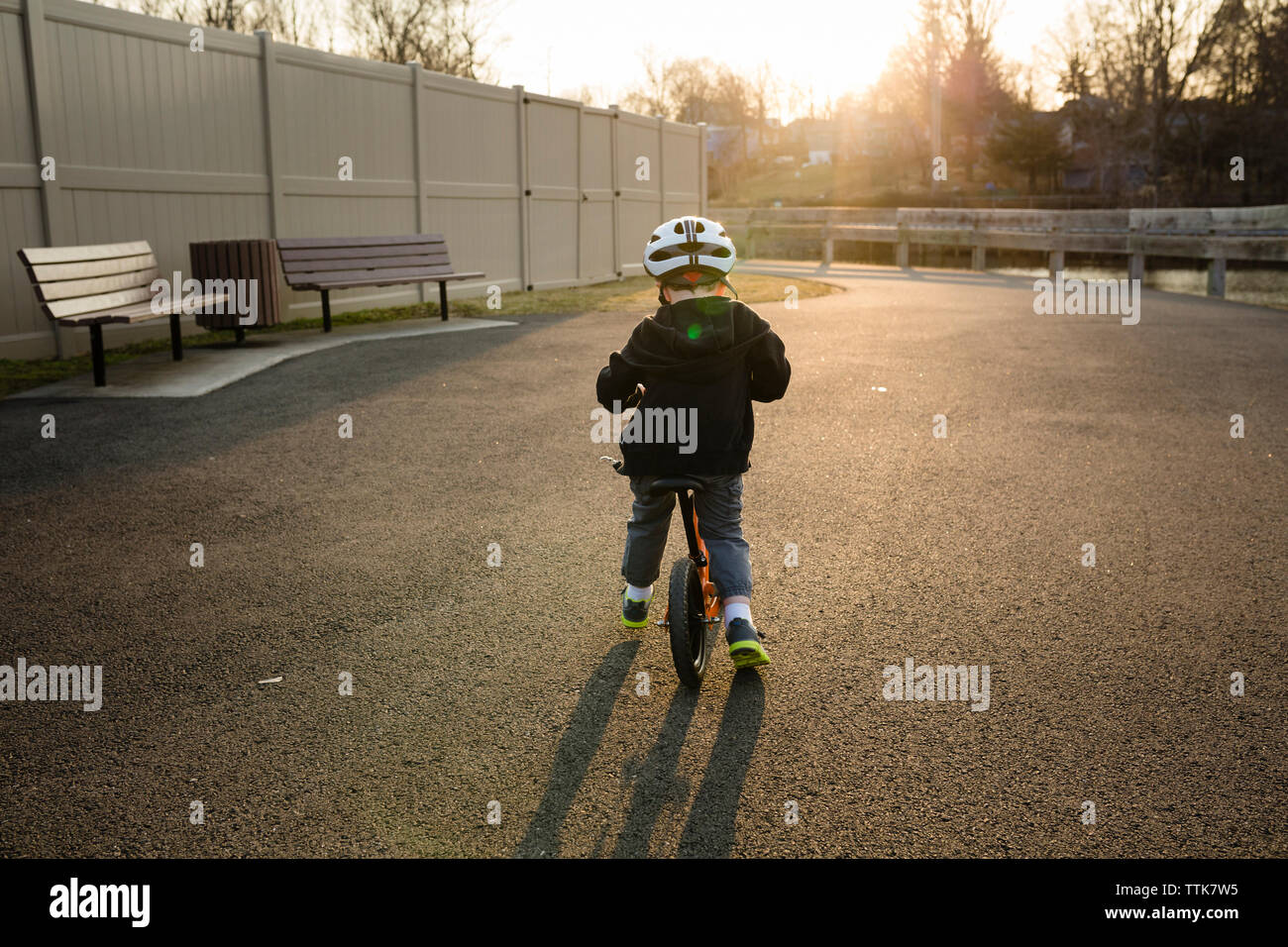Rear view of boy wearing cycling helmet while riding bicycle on road ...