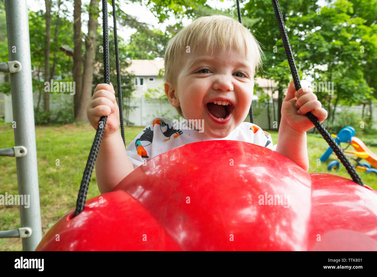 Portrait of cute playful baby boy screaming while swinging on red ...