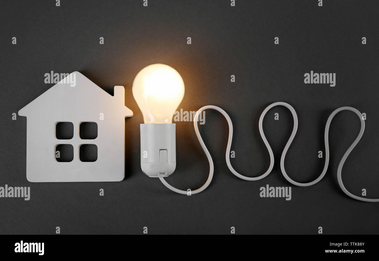 Electric bulb and house on grey background Stock Photo - Alamy