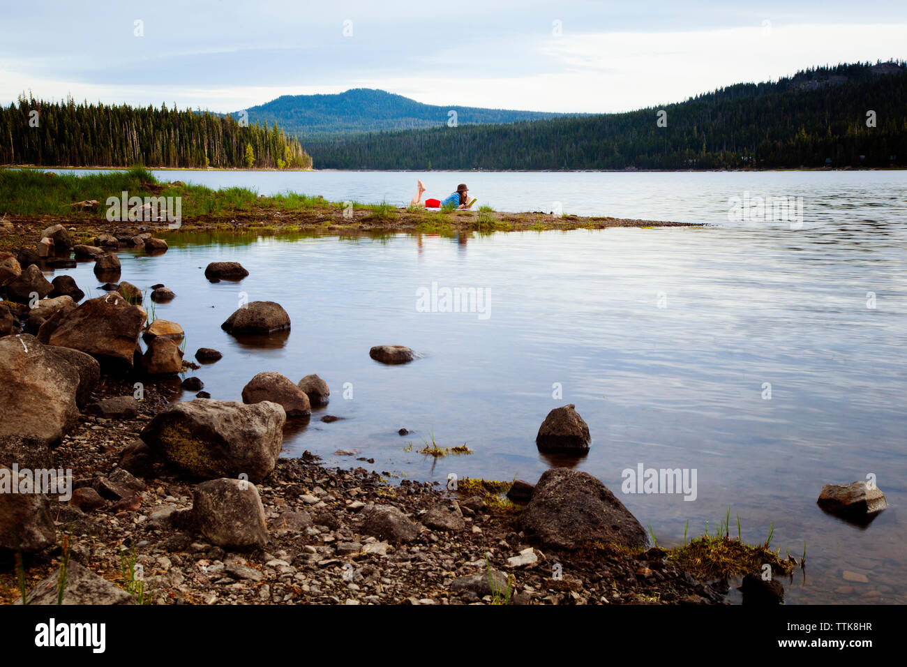 Woman lying on field by Elk Lake against mountains and sky Stock Photo ...