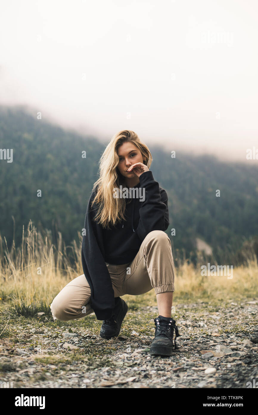 Portrait of confident woman crouching on field against mountain in ...