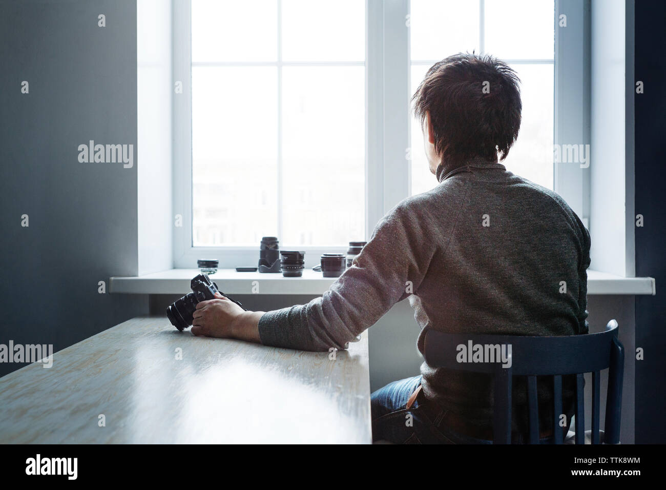 Rear view of male photographer holding camera and sitting on chair ...