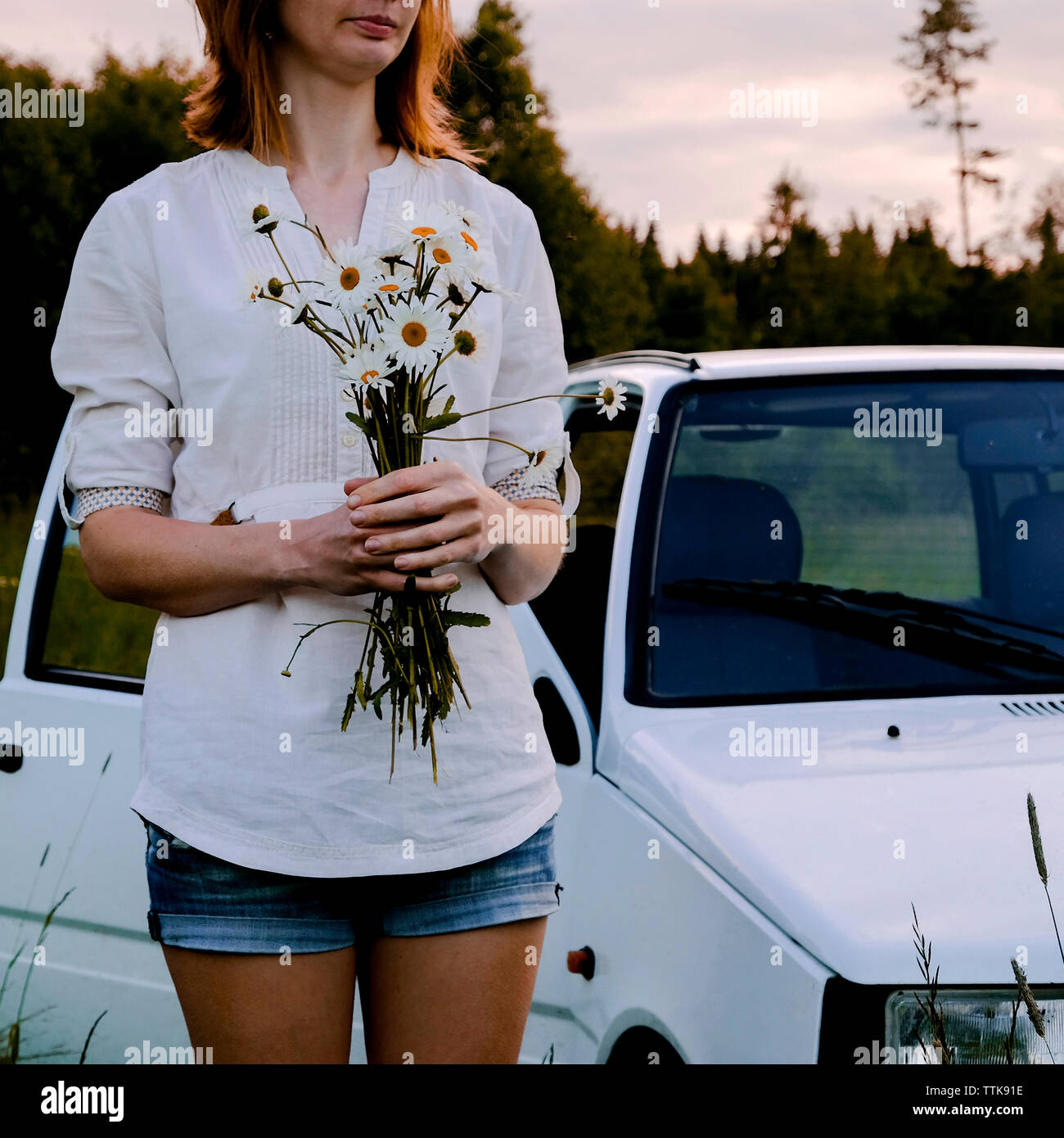 Midsection of woman holding flowers while standing against car on field ...