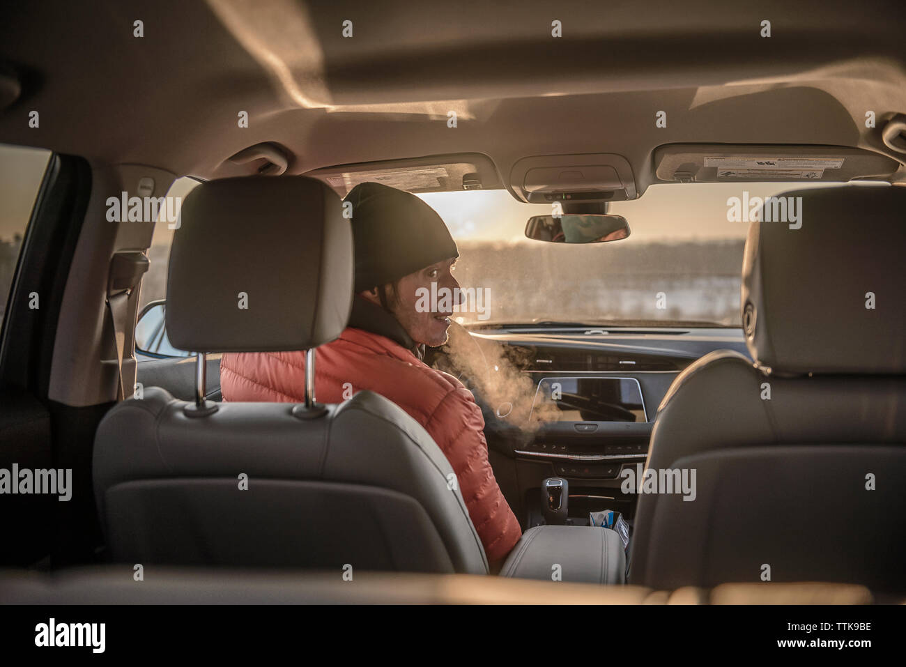 View of man inside luxury car looking back at sunset in cold weather ...