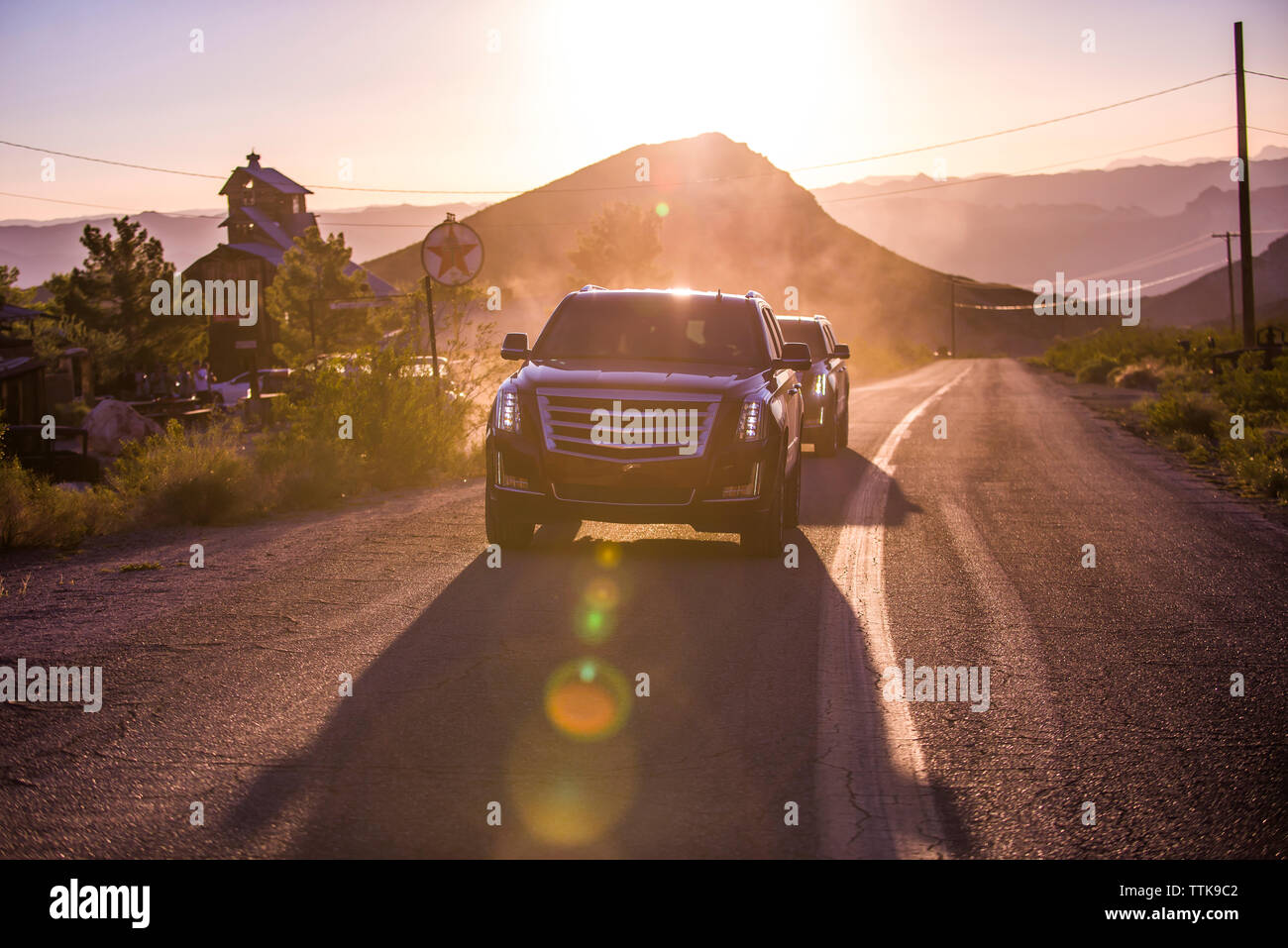 Two luxury car driving on desert road in front of sunset in the desert ...