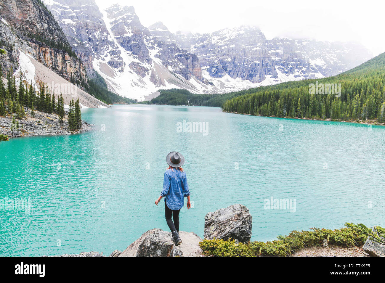 Rear view of woman in fedora hat standing on rock by Moraine Lake ...