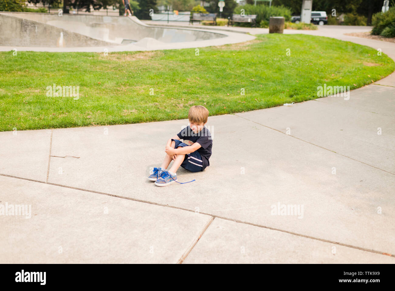 High angle view of sad boy sitting on footpath at park Stock Photo - Alamy