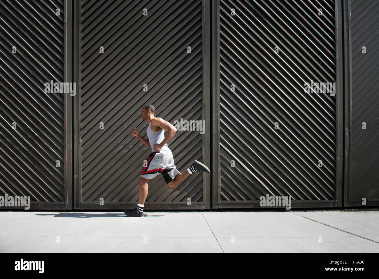 Side view of man running on floor against metal wall Stock Photo - Alamy