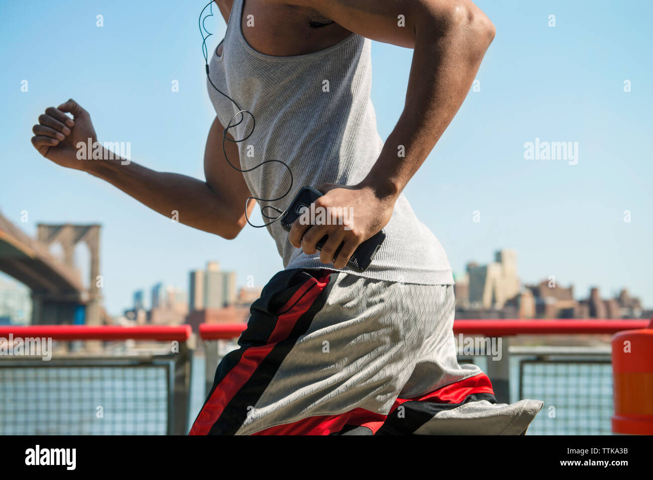 Midsection of man holding smart phone and jogging against sky Stock ...