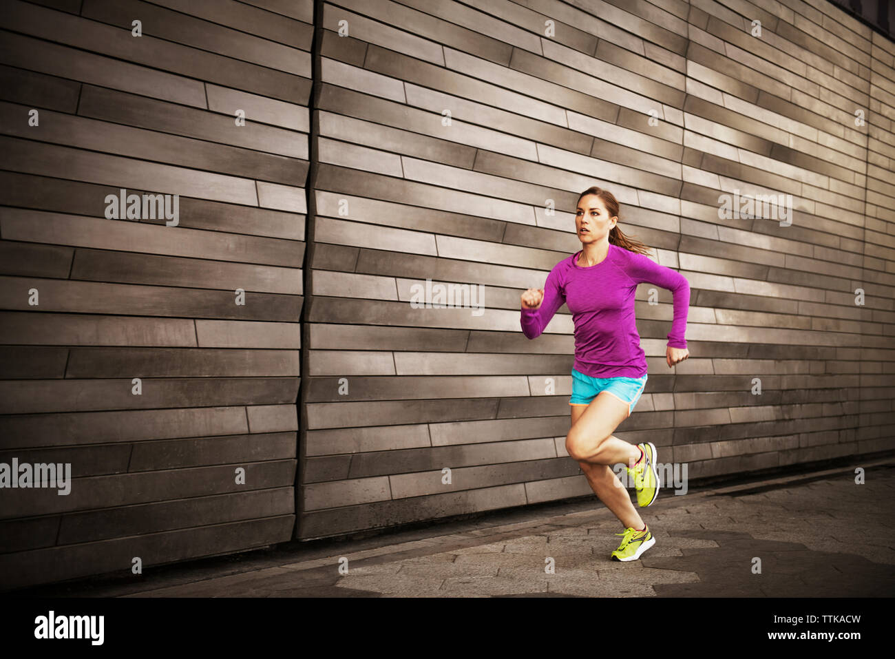 Woman jogging on sidewalk by wall Stock Photo - Alamy