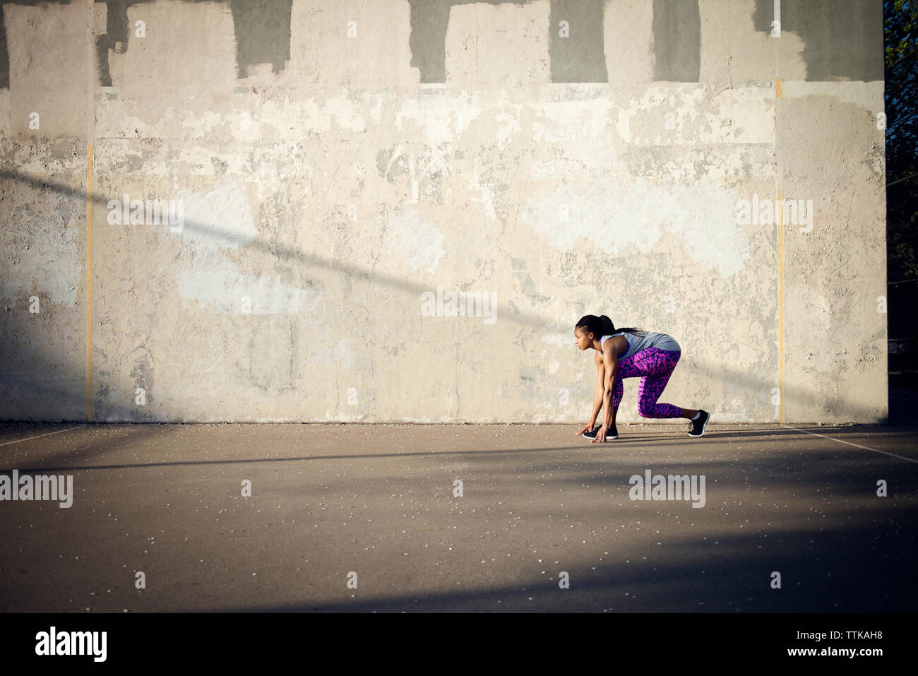 Woman in starting position on street ready to run by wall Stock Photo ...