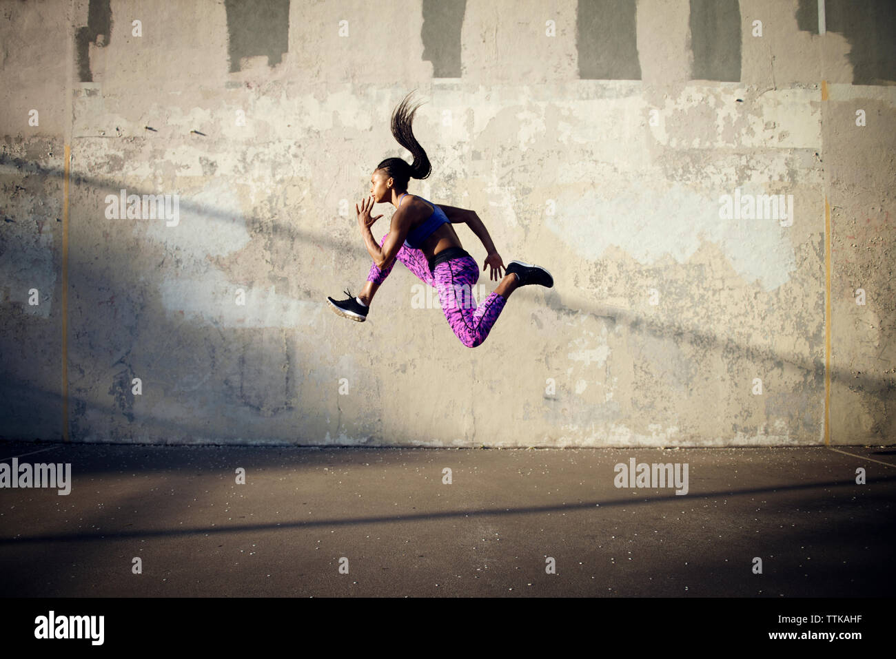 Side view of woman jumping in mid-air against wall Stock Photo - Alamy