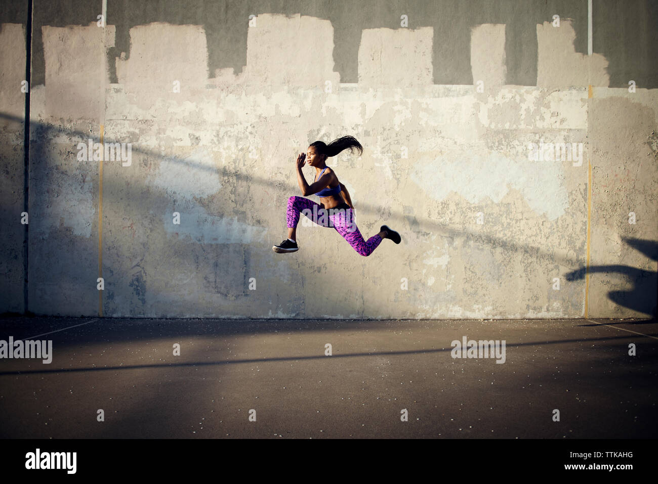 Side view of sportswoman jumping in mid-air against wall Stock Photo ...